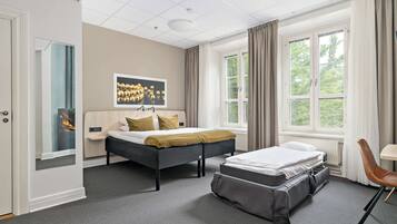 Quarto de hotel moderno com uma cama grande, uma cama menor, uma escrivaninha e uma cadeira.