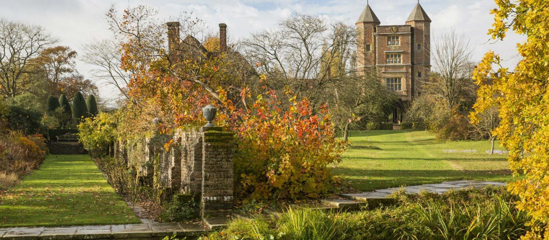 Um edifício histórico com uma torre, rodeado por um jardim bem cuidado e um caminho de pedra que leva à entrada.