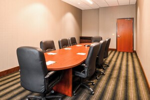 Uma sala de conferências com uma mesa comprida, cadeiras pretas e piso coberto por carpete.
