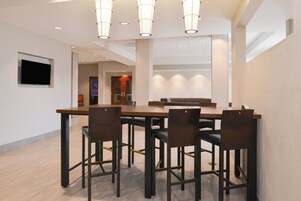 Uma sala de jantar moderna com uma mesa comprida e quatro cadeiras, uma televisão de tela plana na parede e iluminação embutida no teto.