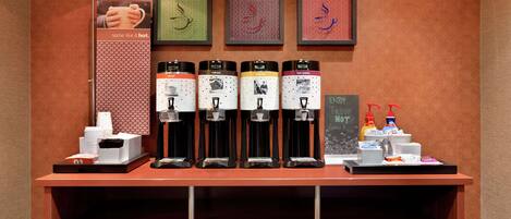 Uma estação de café com vários dispensadores, um painel de cardápio e um pôster emoldurado na parede.