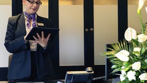 Um balcão de recepção com uma placa de identificação, um tablet e um arranjo de flores.