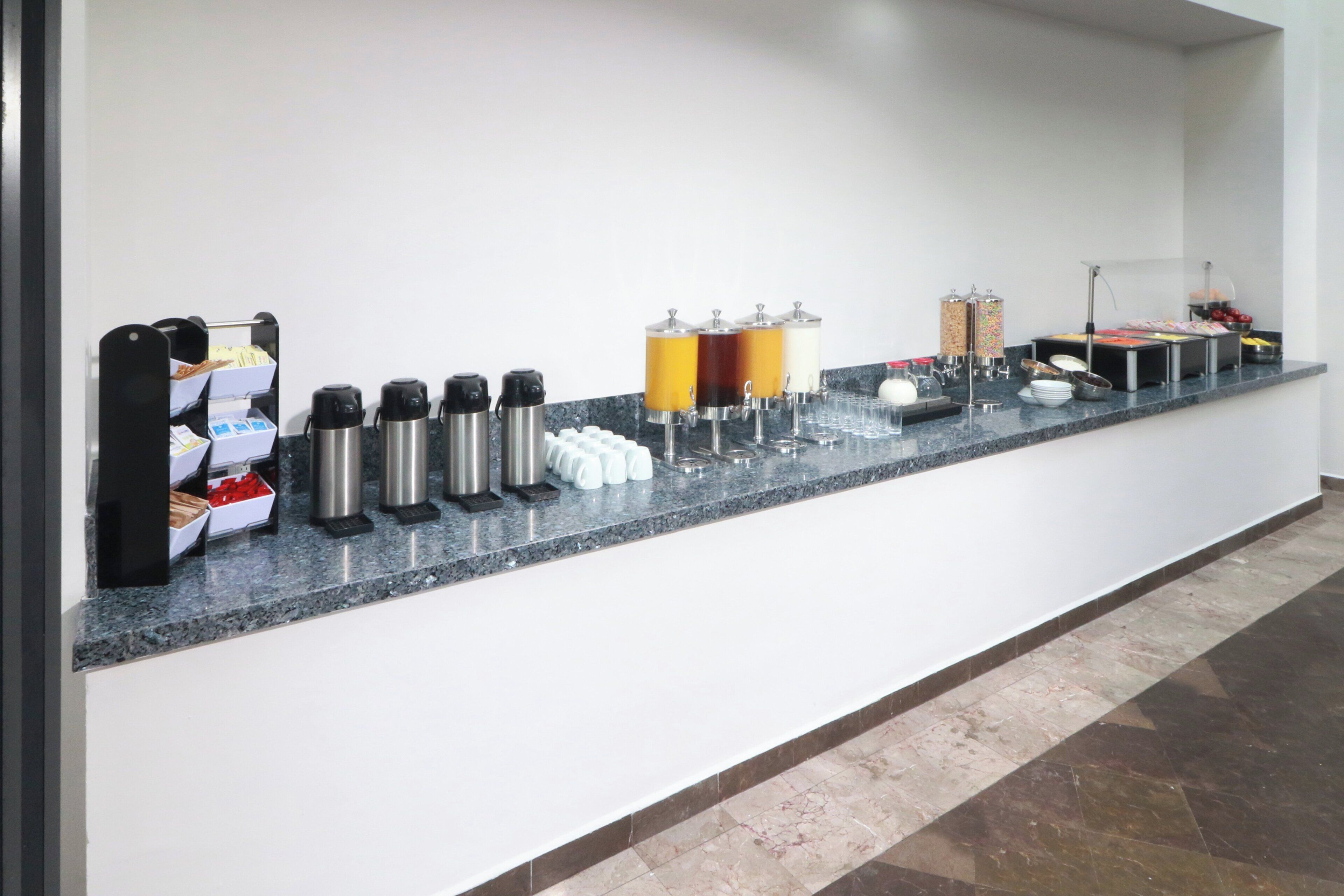 Disposição de buffet com diversos dispensadores de comida e bebida, incluindo máquinas de café e dispensadores de suco.
