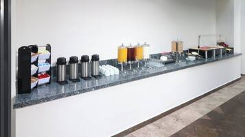 Disposição de buffet com diversos dispensadores de comida e bebida, incluindo máquinas de café e dispensadores de suco.