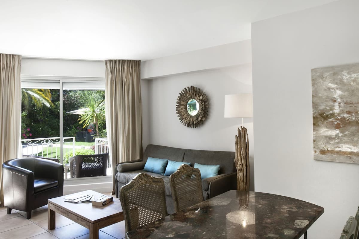 Uma sala de estar com sofá, cadeiras, mesa de centro, mesa de jantar e vista para o exterior através de uma porta deslizante.