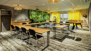 Uma sala de conferências com uma mesa comprida, cadeiras, um projetor e uma parede verde.