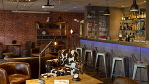 Uma área de bar com cadeiras de couro, uma mesa de madeira e uma parede de tijolos.