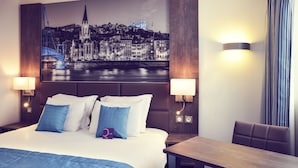 Quarto de hotel com uma cama grande, duas mesas de cabeceira, uma escrivaninha e uma cadeira. Há um mural com vista para a cidade na parede atrás da cama.