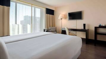 Quarto de hotel com cama grande, escrivaninha, cadeira, televisão e janela com cortinas.