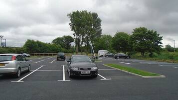 Estacionamento com vários carros e uma grande árvore ao fundo.