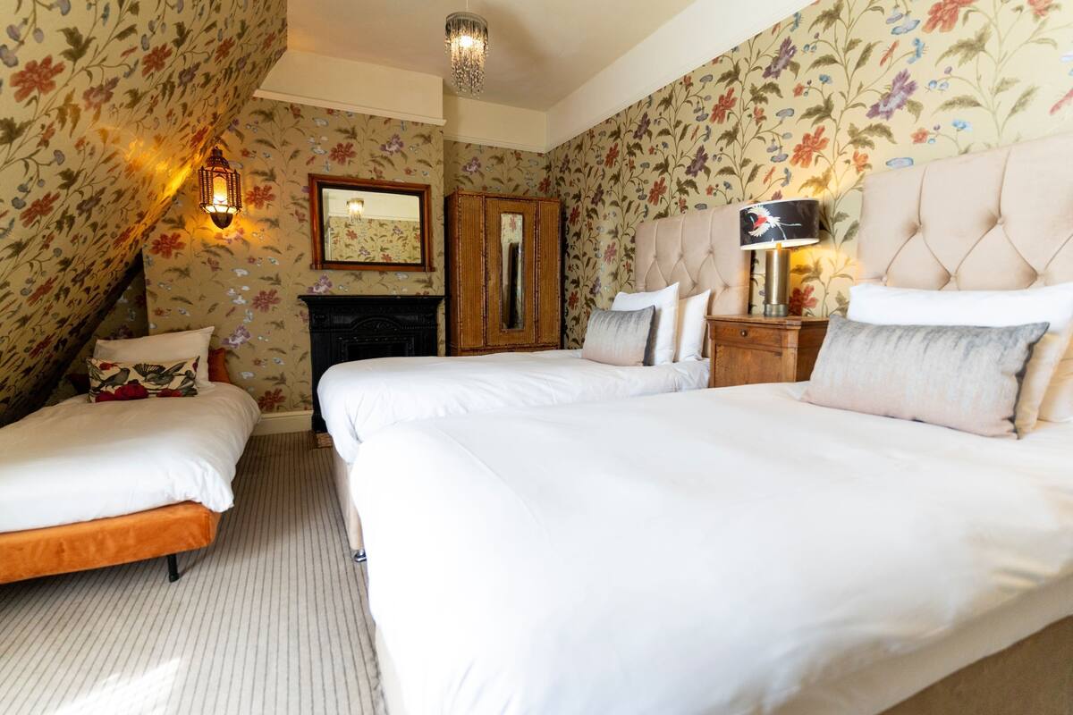 Quarto com duas camas, um espelho, lareira e papel de parede floral.