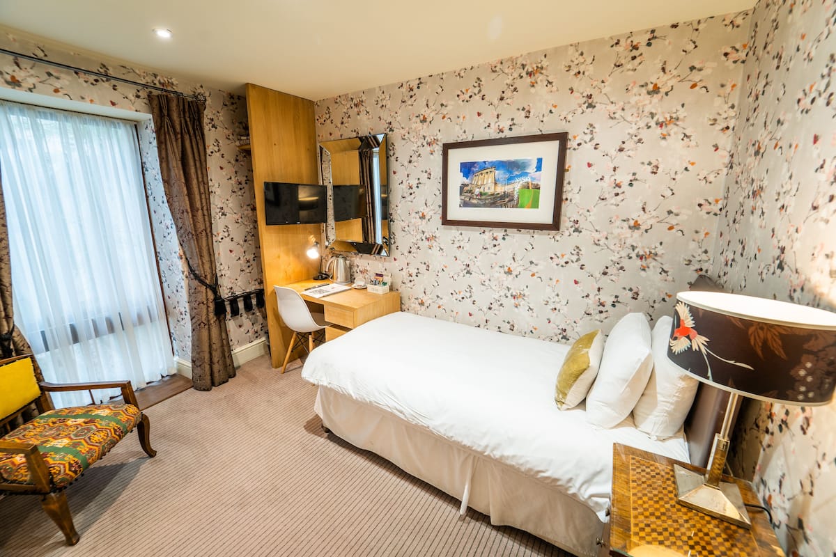 Quarto de hotel com cama, escrivaninha, cadeira e um espelho grande.