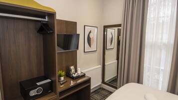Quarto de hotel com cama, escrivaninha com rádio, espelho e janela com cortinas.