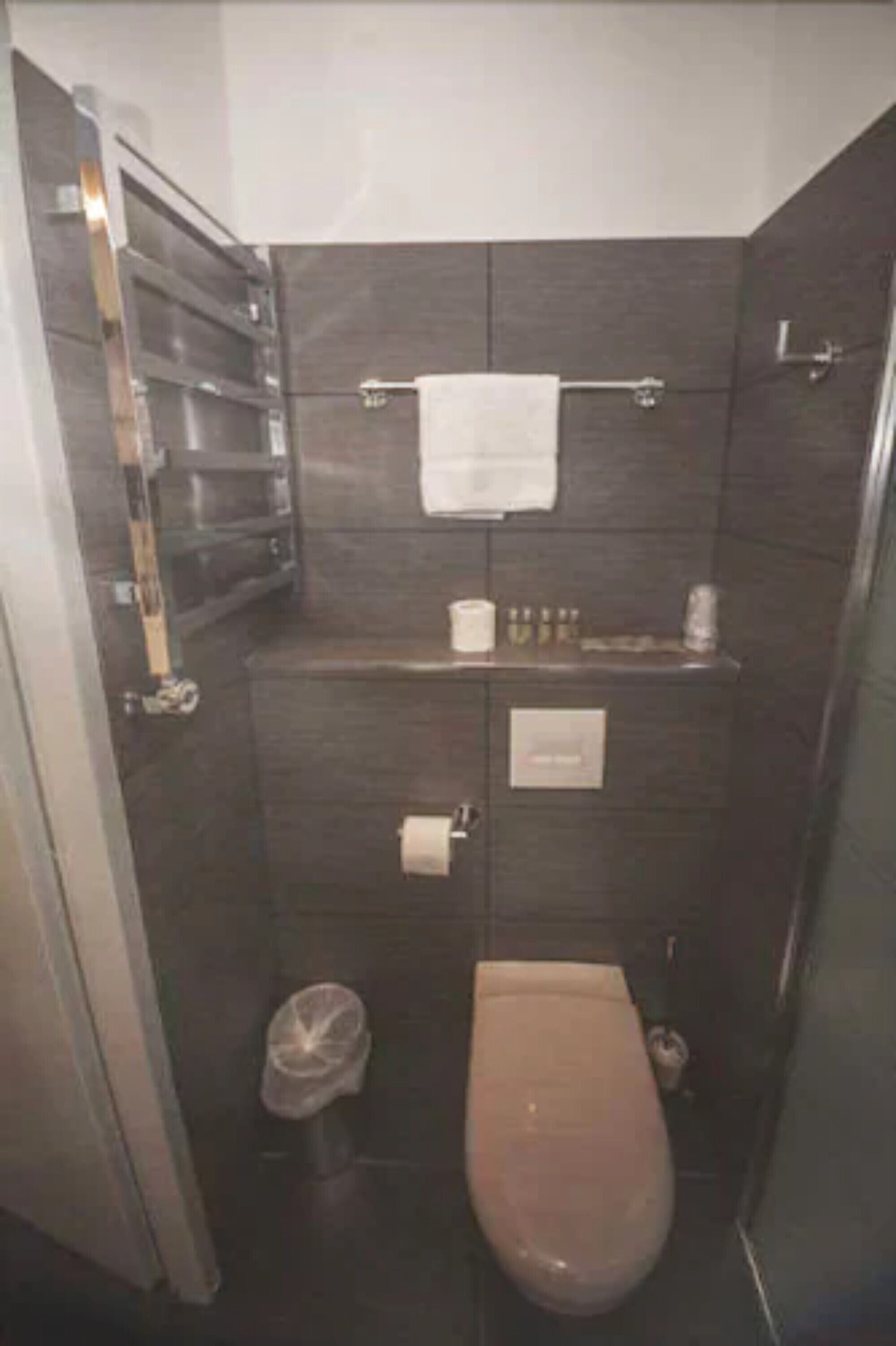 Um banheiro compacto com vaso sanitário, uma lixeira pequena e um porta-toalhas.