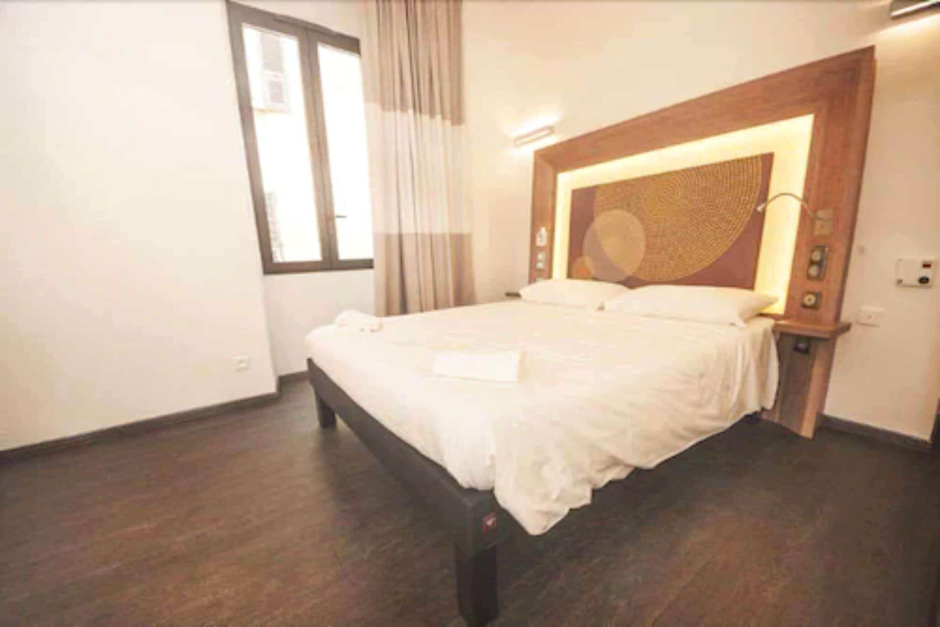 Uma cama bem arrumada com cabeceira de madeira, mesa de cabeceira e uma janela com cortinas.