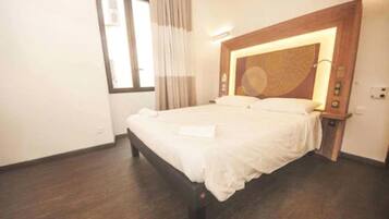 Uma cama bem arrumada com cabeceira de madeira, mesa de cabeceira e uma janela com cortinas.