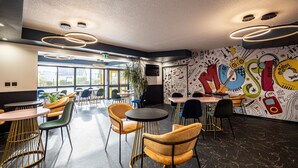 Um café moderno com mesas redondas, cadeiras coloridas e um mural na parede com notas musicais e instrumentos.