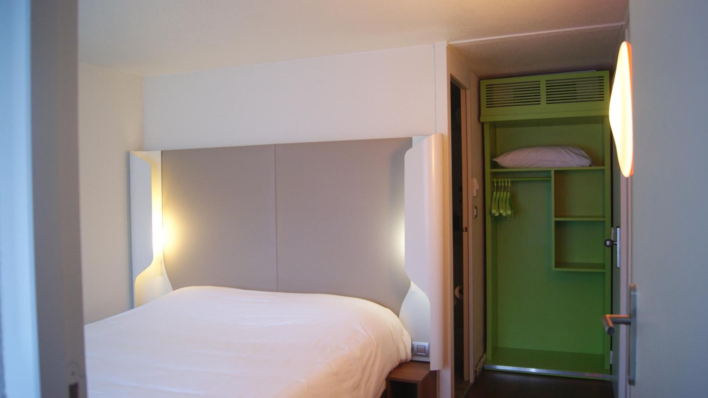 Quarto de hotel com uma cama, um guarda-roupa verde e uma mesa de cabeceira.