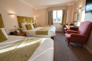 Quarto de hotel com duas camas, uma escrivaninha, uma cadeira, uma televisão e uma janela com cortinas.