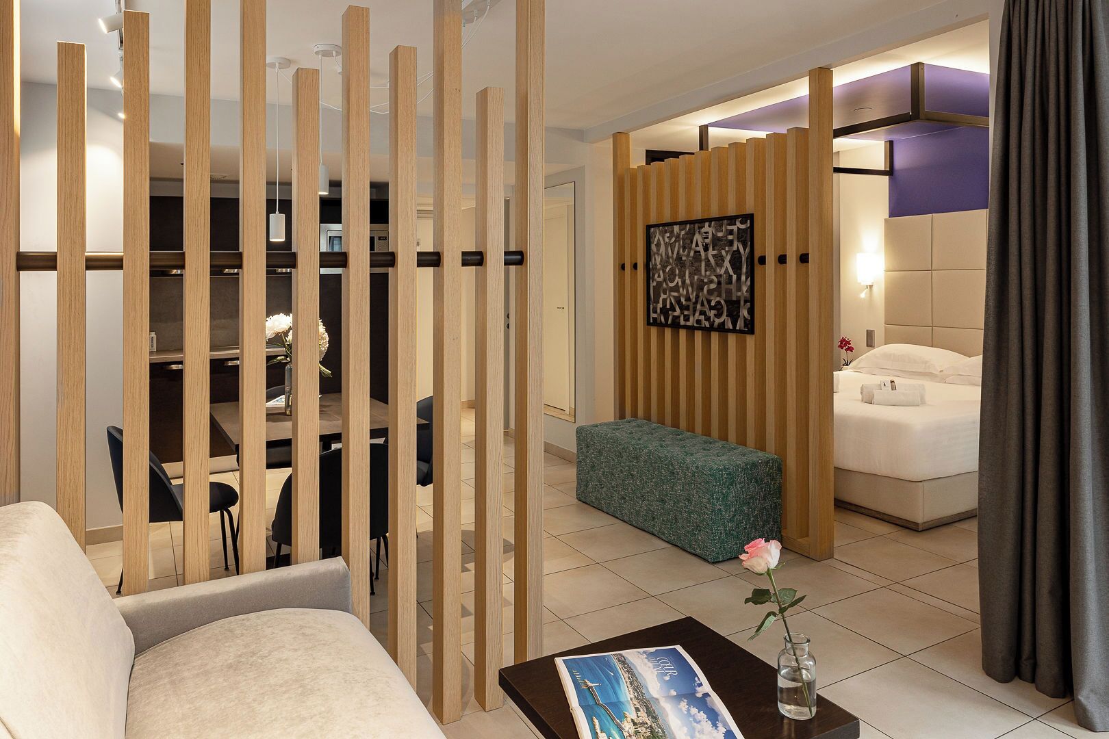 Quarto de hotel moderno com sofá, área de refeições, cama e painel decorativo na parede.