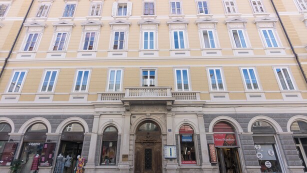Um edifício de vários andares com estilo arquitetônico clássico, com janelas em arco e uma entrada central com porta decorativa.