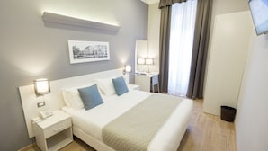 Quarto de hotel bem arrumado, com cama, mesas de cabeceira, escrivaninha e espelho.