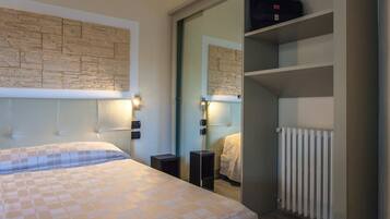 Quarto com cama, mesas de cabeceira, radiador e guarda-roupa com prateleiras.