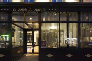 Entrada de hotel com placa indicando 'Le Relais du Marais' e sinalização de acessibilidade para pessoas com deficiência.