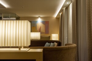 Quarto de hotel moderno com sofá marrom, mesa lateral e um quadro na parede.