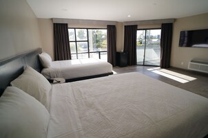 Quarto de hotel com duas camas, uma televisão de tela plana, uma janela grande e uma porta deslizante para área externa.