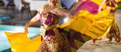 Apresentação de dança tradicional com dois dançarinos em trajes elaborados, com uma piscina e área de estar ao ar livre ao fundo.