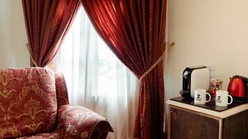 Um quarto com um sofá vermelho estampado, um armário de madeira com uma cafeteira e duas chávenas em cima.