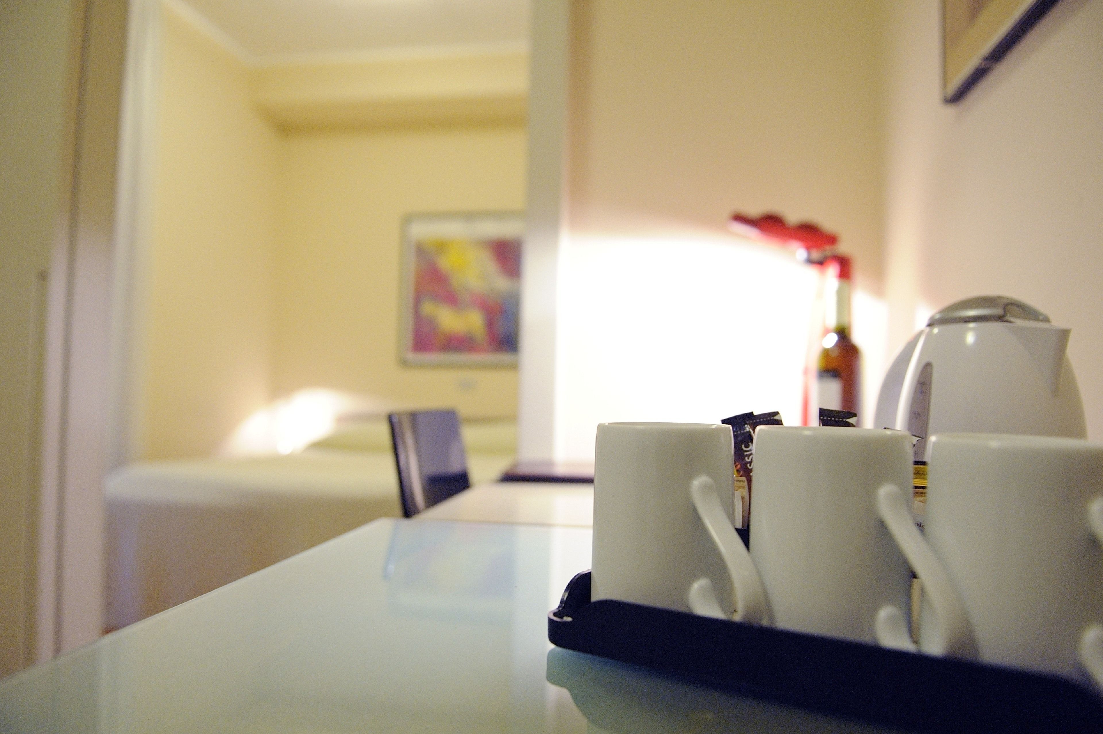 Quarto de hotel com uma mesa de jantar posta com xícaras brancas e uma cafeteira.