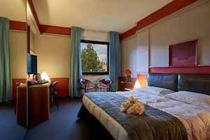 Quarto de hotel com cama, escrivaninha, cadeiras e janela com vista.