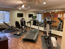 Academia com aparelhos de cardio, um espelho e piso de madeira.