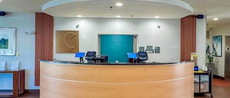 Uma receção com design curvo, duas estações de trabalho com computadores, uma parede azul e um relógio.