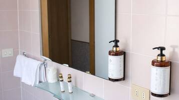 Casa de banho com lavatório branco, prateleira de vidro com produtos de higiene, espelho e porta-toalhas.