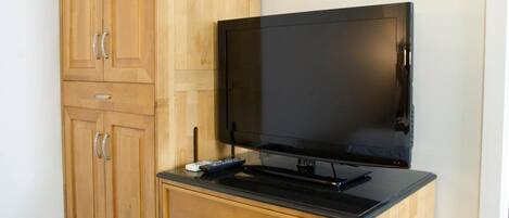 Quarto com guarda-roupa de madeira, televisão de tela plana em suporte preto e piso coberto por carpete.