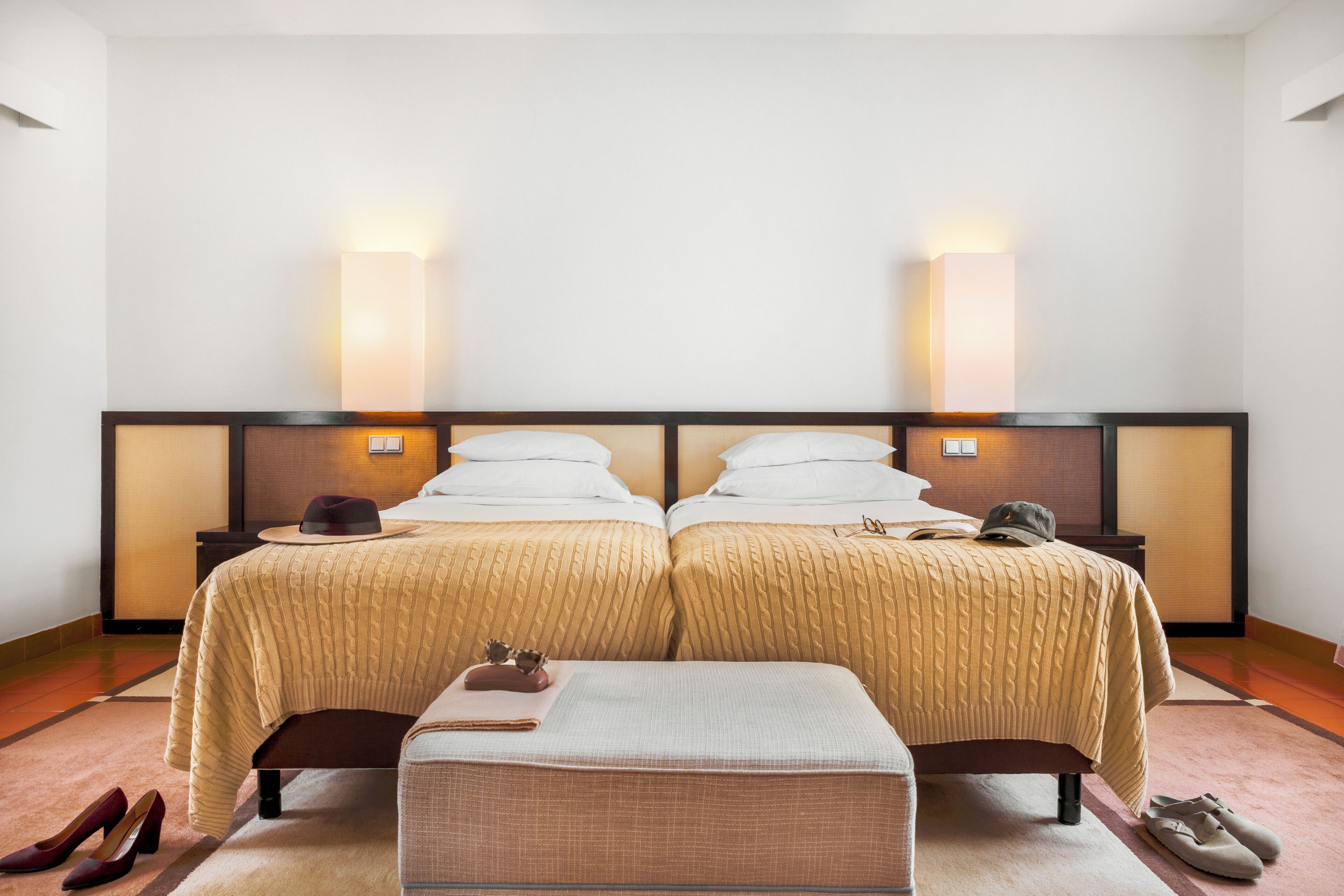 Uma cama de casal com cabeceira de madeira, duas mesas de cabeceira e um criado-mudo.