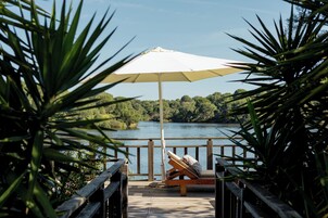 Um deck de madeira com uma espreguiçadeira e guarda-sol, com vista para um lago.