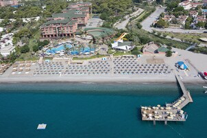 Vista aérea de um resort à beira-mar, com uma piscina grande, guarda-sóis na praia e um píer.
