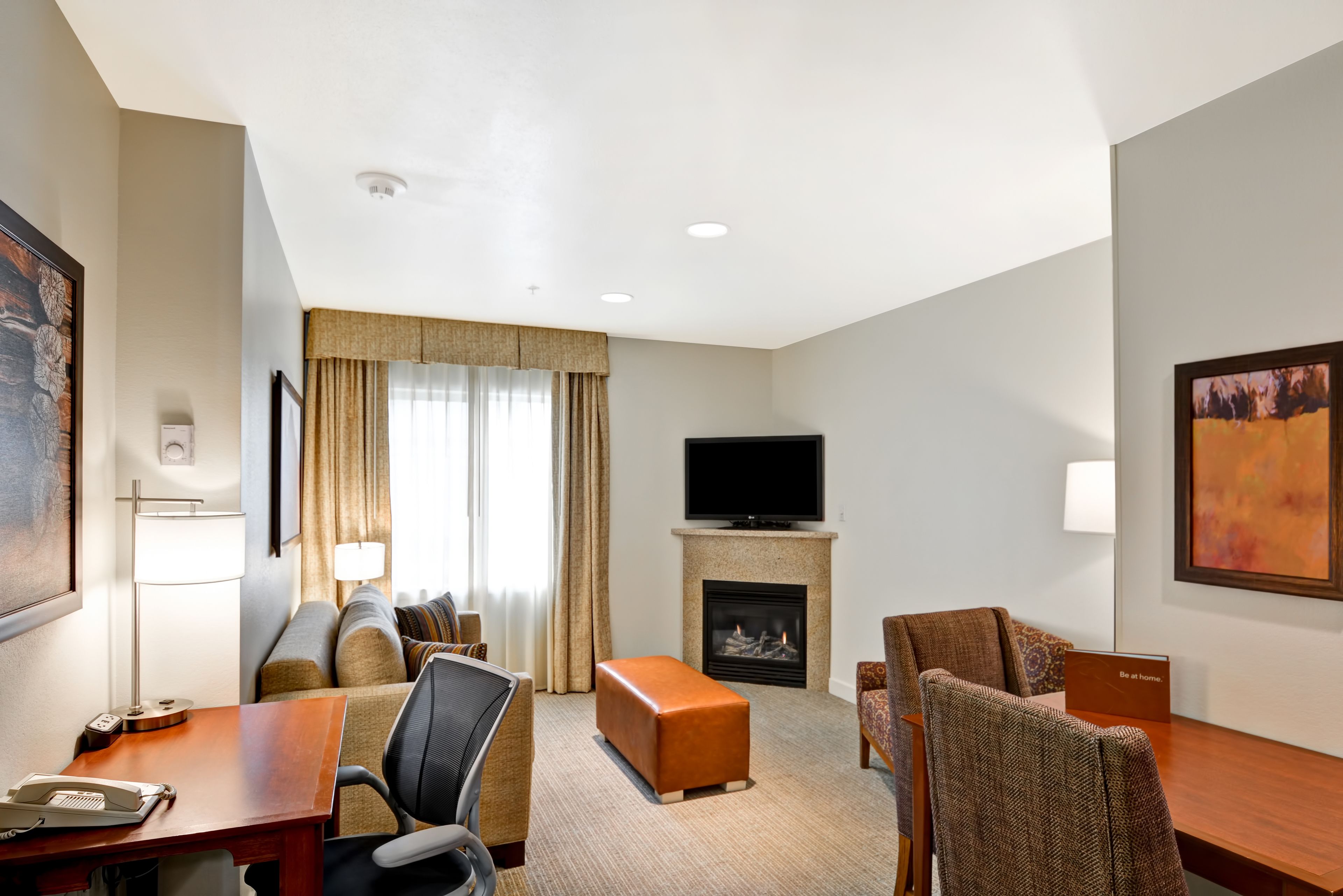 Quarto de hotel com sofá, escrivaninha com telefone, televisão sobre lareira e mesa de jantar com cadeiras.
