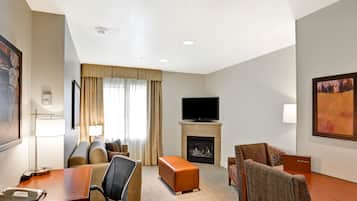 Quarto de hotel com sofá, escrivaninha com telefone, televisão sobre lareira e mesa de jantar com cadeiras.