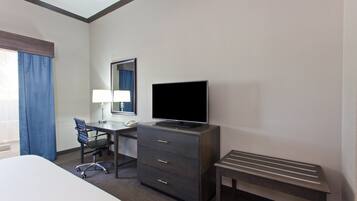 Quarto de hotel com cama, escrivaninha com computador, televisão, cadeira e uma pequena mesa.