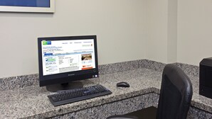 Um computador de mesa com monitor exibindo um site de reservas de hotel, teclado, mouse e cadeira de escritório preta.