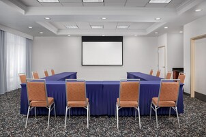 Uma sala de conferência com uma mesa comprida, cadeiras, uma tela de projetor e uma porta.