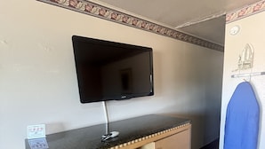 Quarto com televisão de tela plana fixada em um armário de madeira, um centro de passar roupa azul e piso estampado.