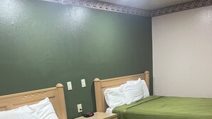 Duas camas de solteiro com roupa de cama verde, um cabeceira de madeira, uma mesa de cabeceira com um relógio e uma parede lisa.