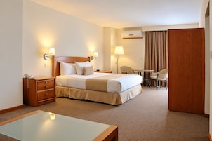 Quarto de hotel com cama, mesas de cabeceira, escrivaninha e cadeira.
