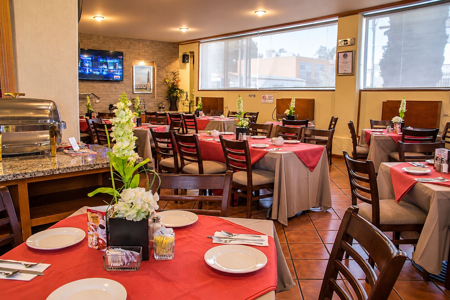 Um restaurante com várias mesas, cada uma disposta com pratos, talheres e um vaso de flores.